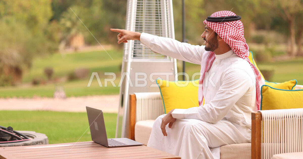 A Saudi Arabian Gulf man pointing to something, using a laptop, working ...