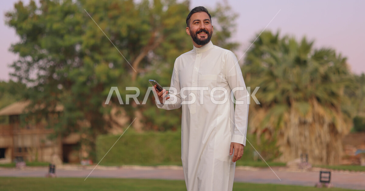 A Saudi Arabian Gulf man wandering in a public park, using a mobile ...