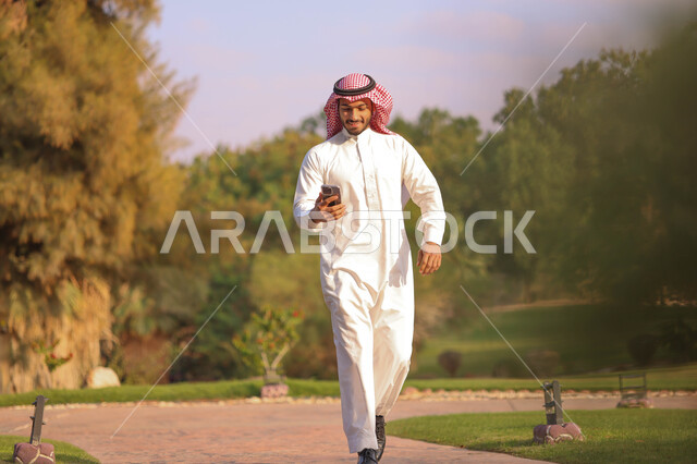 A Saudi Arabian Gulf man wandering in a public park, using a mobile ...