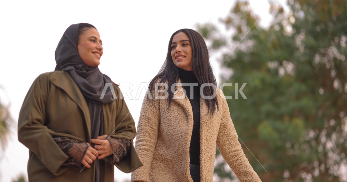 Two Saudi Arabian Gulf female friends strolling in a public park ...