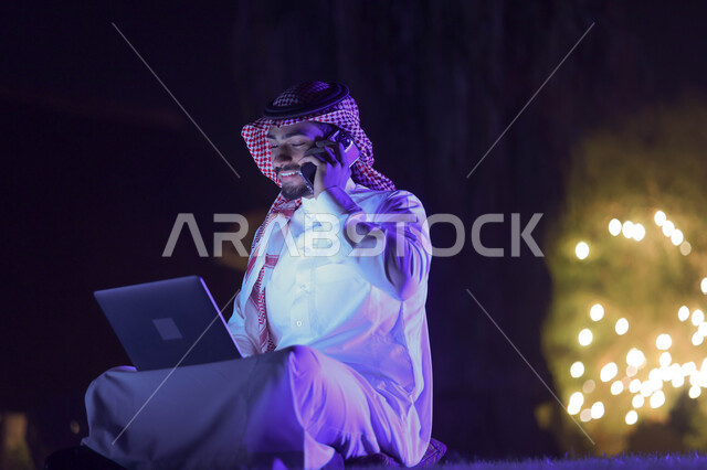 A Saudi Arabian Gulf man using a laptop, making a phone call, browsing ...