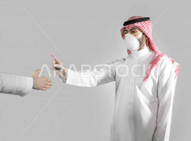 Portrait of a Saudi Arabian Gulf youth wearing a mask, raising his hand ...