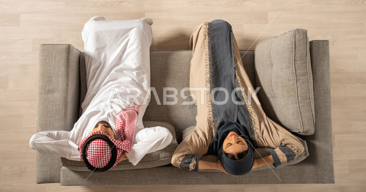 صورة من الاعلى لزوجان عربيان خليجيان سعوديان يسترخيان على الاريكة