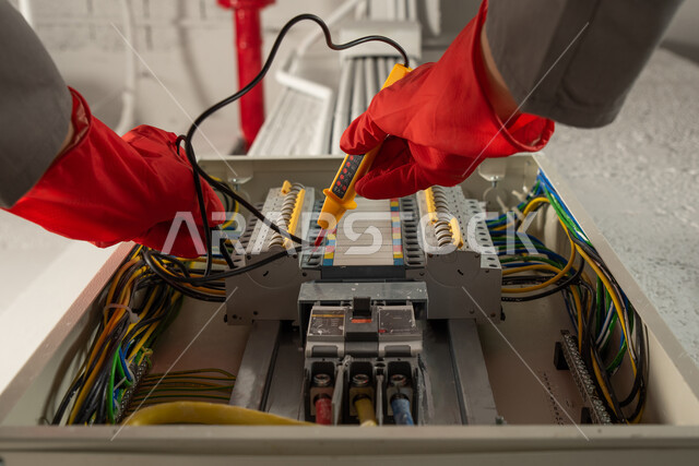 An electrician wearing electrical insulation gloves, using an ammeter ...