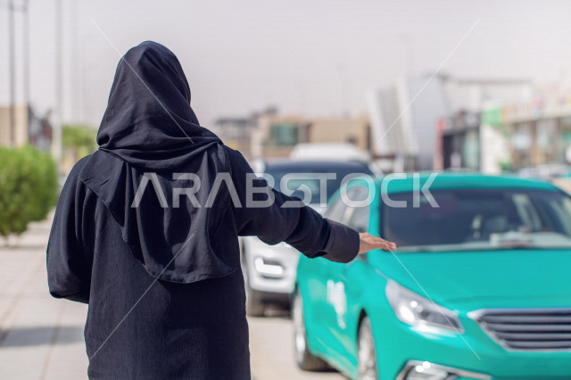 A Saudi Arabian Gulf woman preparing to ride a taxi, using the green ...