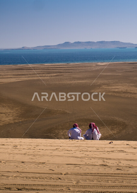 صورة من الخلف لرجلان عربيان خليجيان قطريان يجلسان على تل رملي مطل على ...