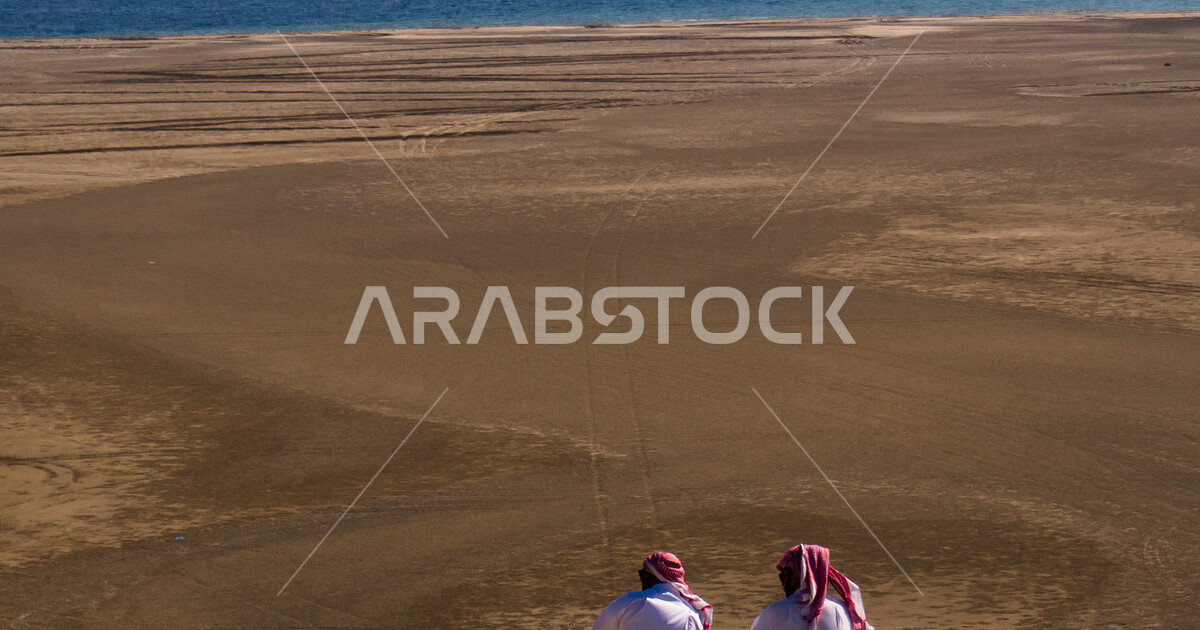 صورة من الخلف لرجلان عربيان خليجيان قطريان يجلسان على تل رملي مطل على ...