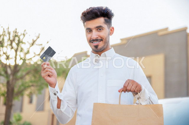 A smiling Saudi Arabian Gulf young man holding a delivery parcel and ...
