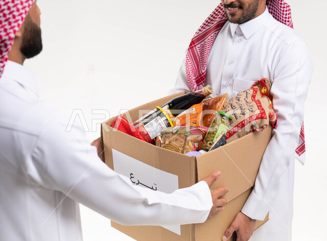 A close-up of two Saudi Arabian Gulf men preparing a food box, donating ...