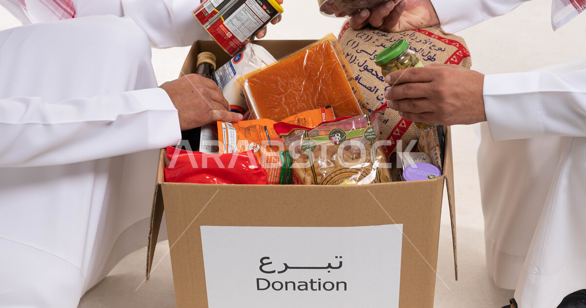 A close-up of two Saudi Arabian Gulf men placing food supplies in a ...