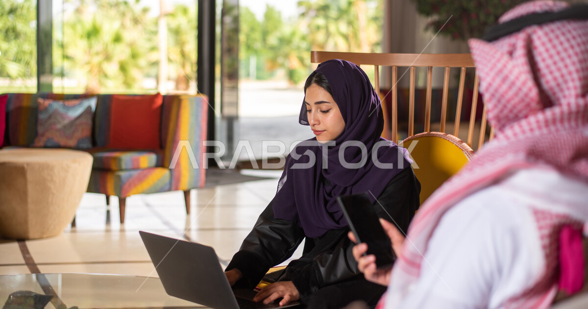 Using a laptop and mobile phone, a Saudi Arabian Gulf man wearing ...