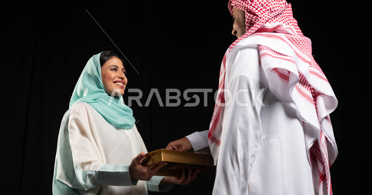 Portrait of a Saudi Arabian Gulf woman serving Eid sweets to guests ...