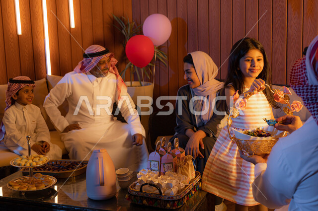 Family visits and gatherings, a close-up of a Saudi Gulf Arab girl serving chocolate and Eid ...