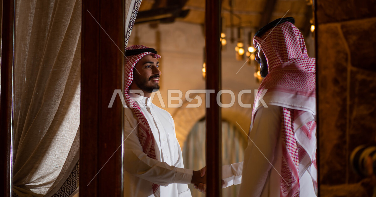 Greetings and peace, two Saudi Arabian Gulf men shaking hands happily ...