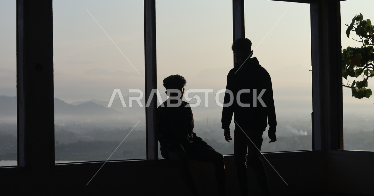 Silhouette of two men standing in front of the window inside the ...