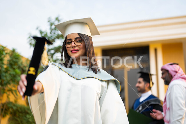 A young Saudi Arabian Gulf woman wears graduation clothes and holds a ...