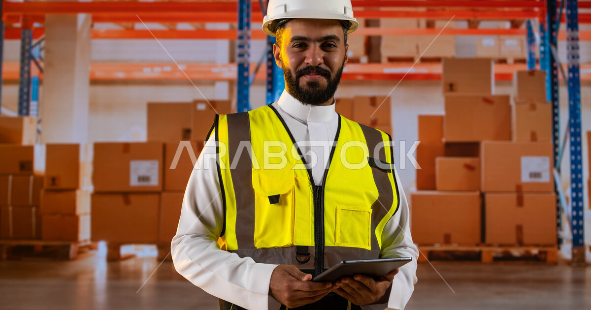 A Saudi Arabian Gulf storekeeper holding a tablet in his hand looking ...