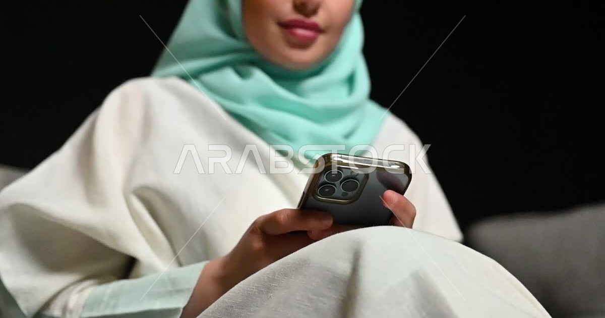 Close-up of a veiled Saudi Arabian Gulf woman using a mobile phone ...
