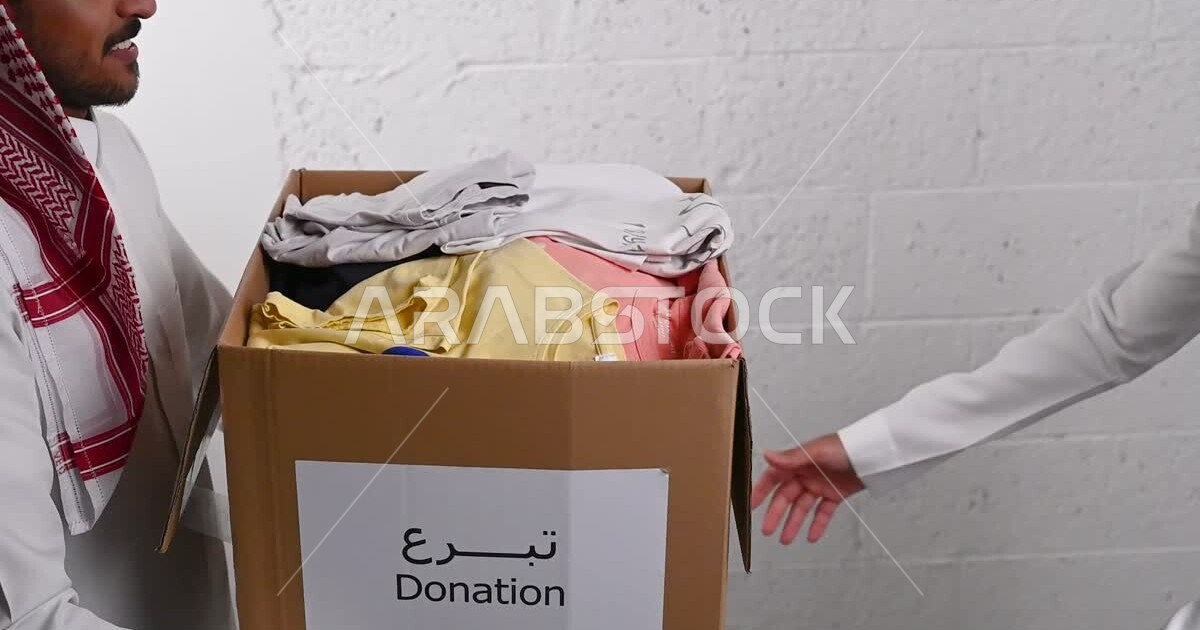 Close-up of a Saudi Gulf man donating a box of clothes, two Saudi men ...