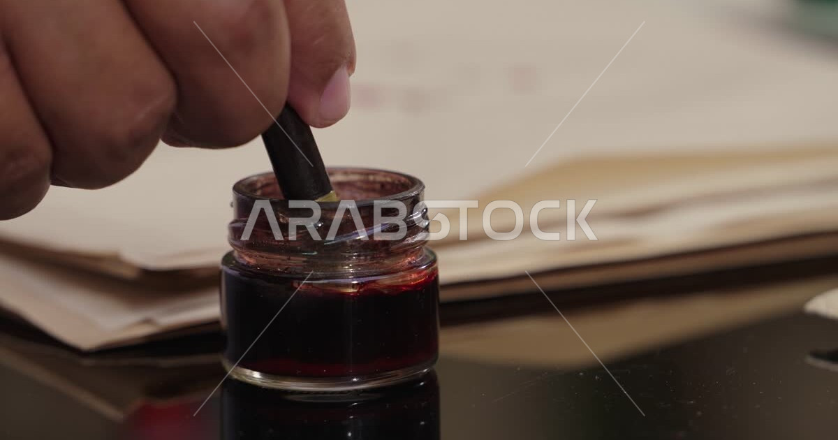 Close-up of the hand of an Arab calligrapher placing a quill in an ink ...