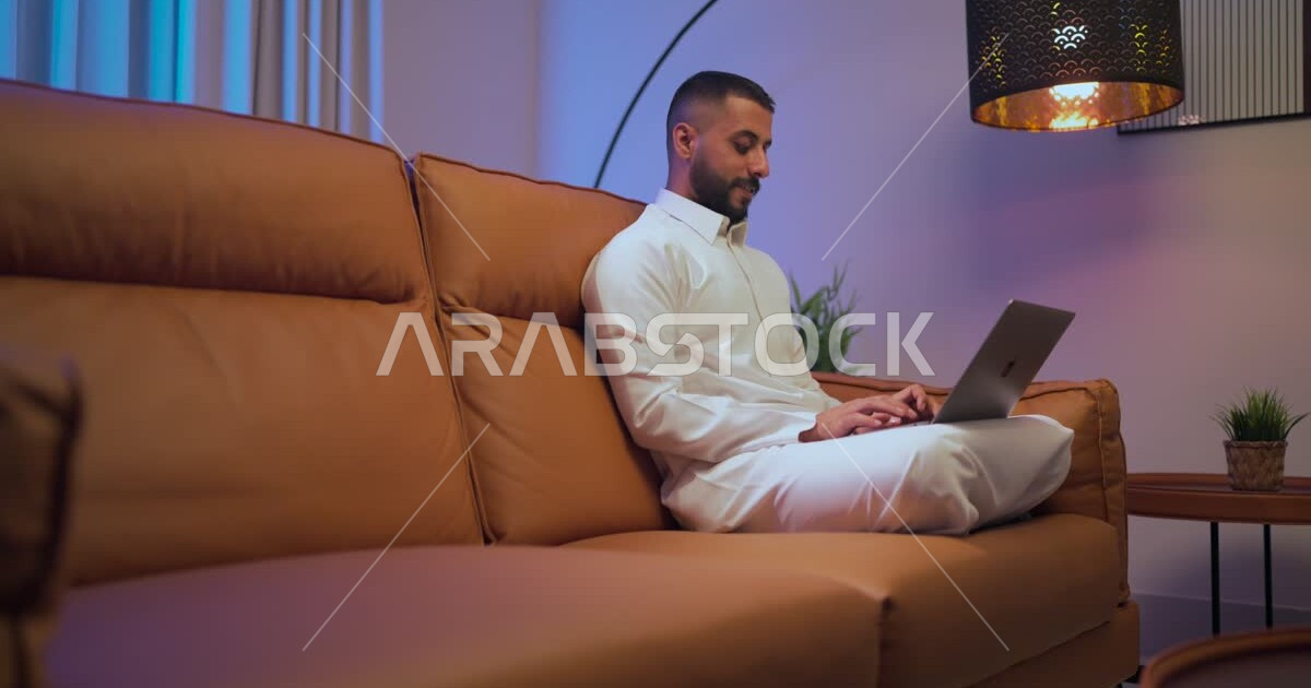 Working remotely using a laptop, a Saudi Arabian Gulf man sitting in ...