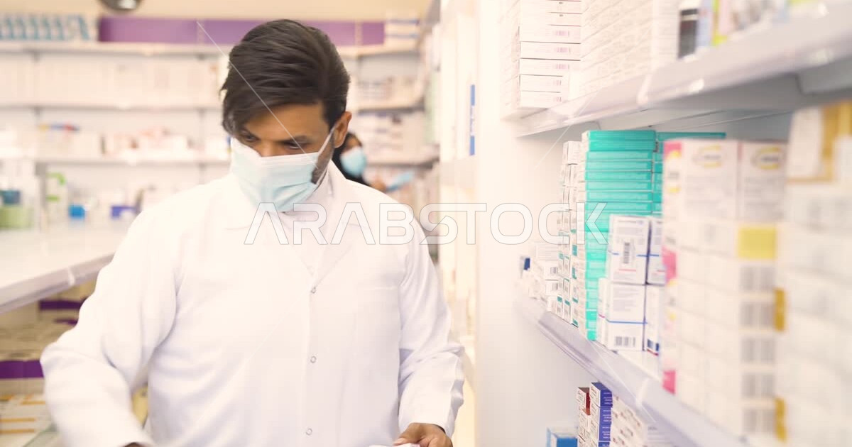 A Saudi Gulf pharmacist working in the pharmacy, wearing a mask to ...