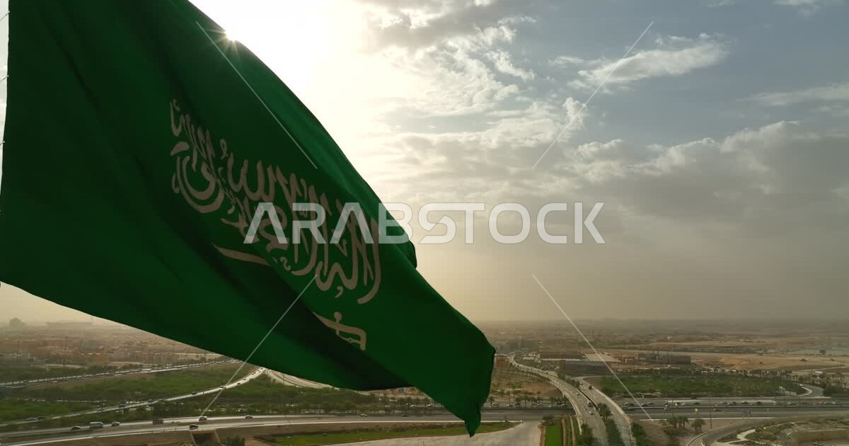Saudi flag pole in Diriyah, trees and green plants, car traffic in the ...