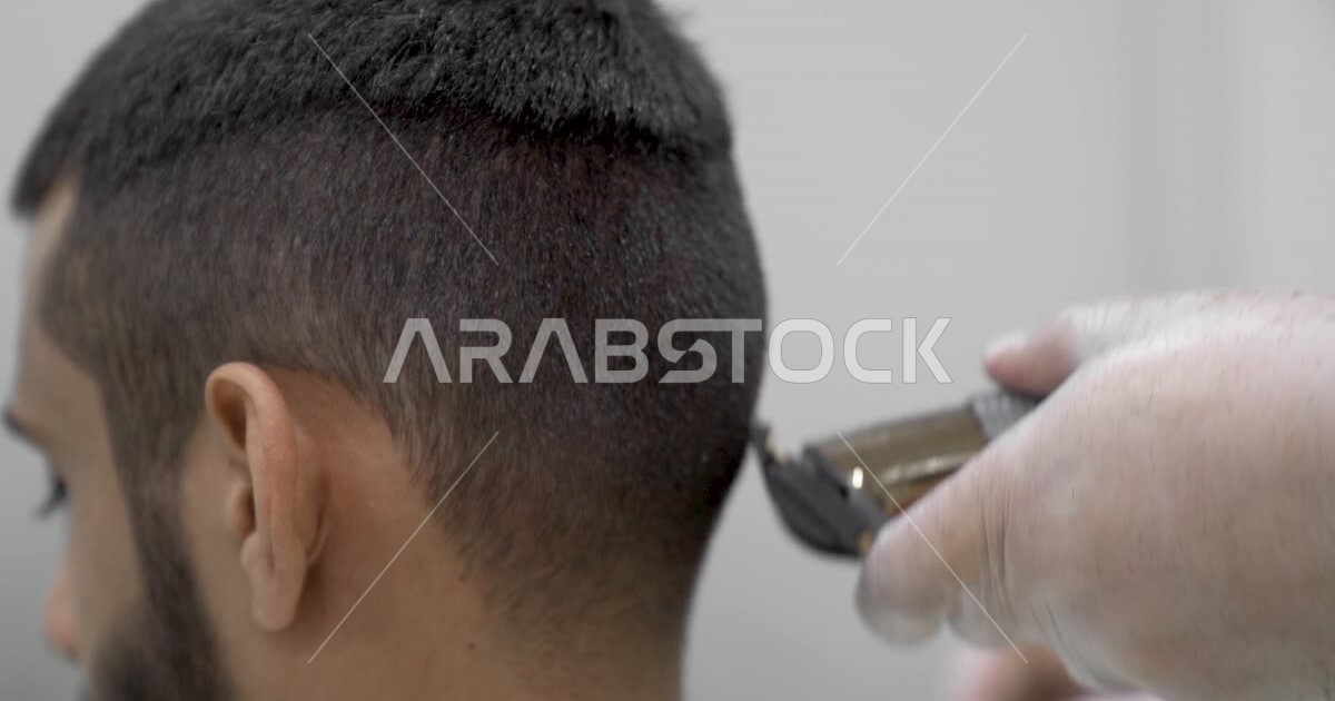 A Saudi Arabian Gulf man visits a barber shop. The barber uses the ...