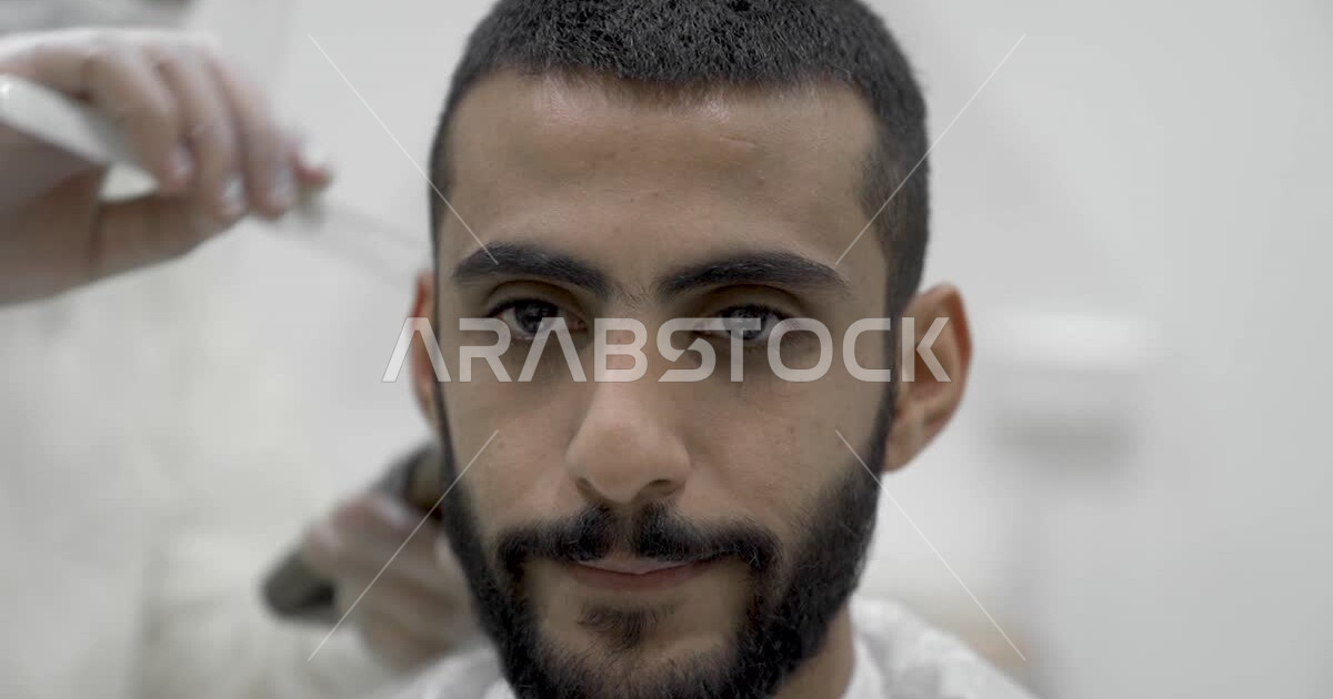 A Saudi Arabian Gulf man visits a barber shop. The barber uses the ...