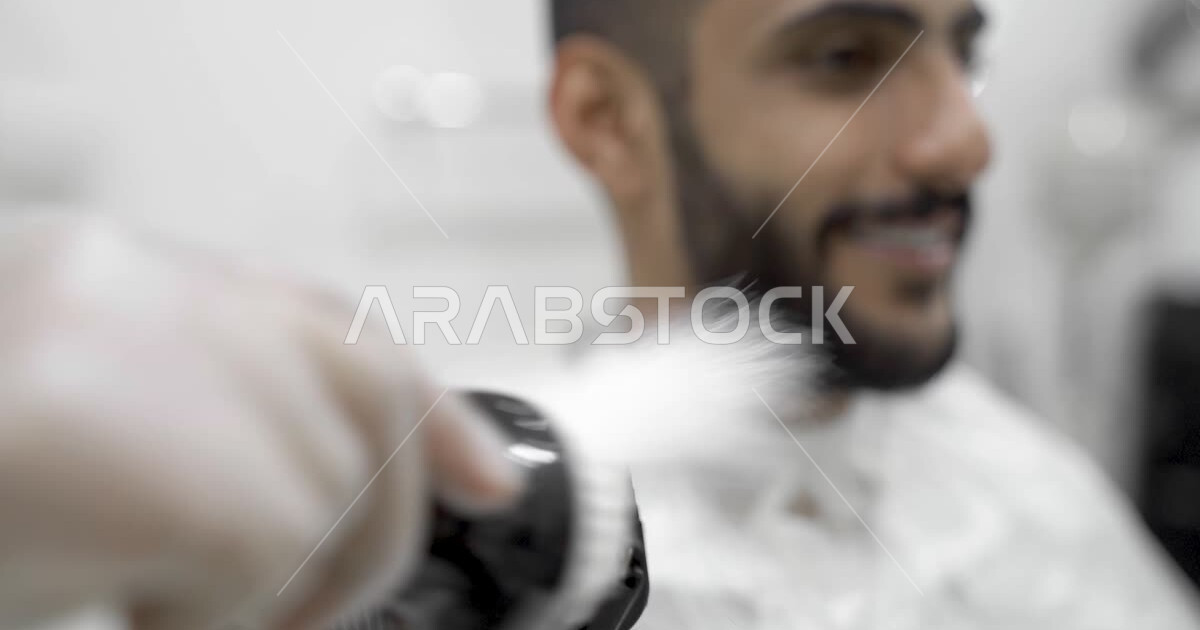 A Saudi Arabian Gulf man visits a barber shop. The barber uses the ...