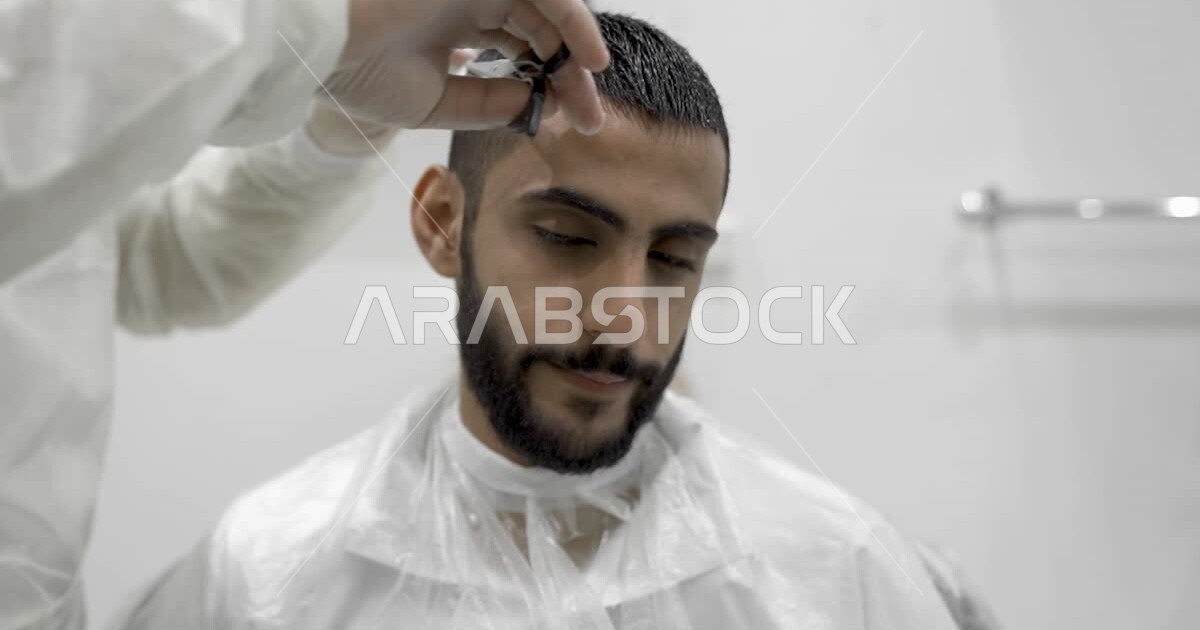 A Saudi Arabian Gulf man visits a barber shop. The barber uses the ...