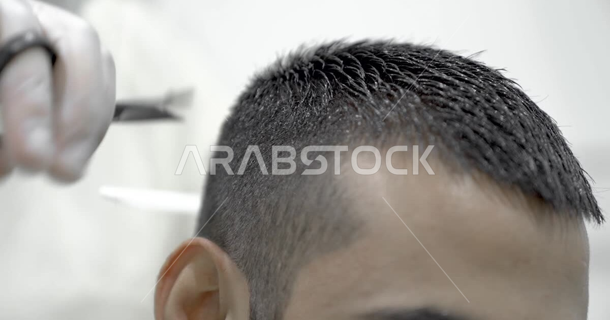 A Saudi Arabian Gulf man visits a barber shop. The barber uses the ...