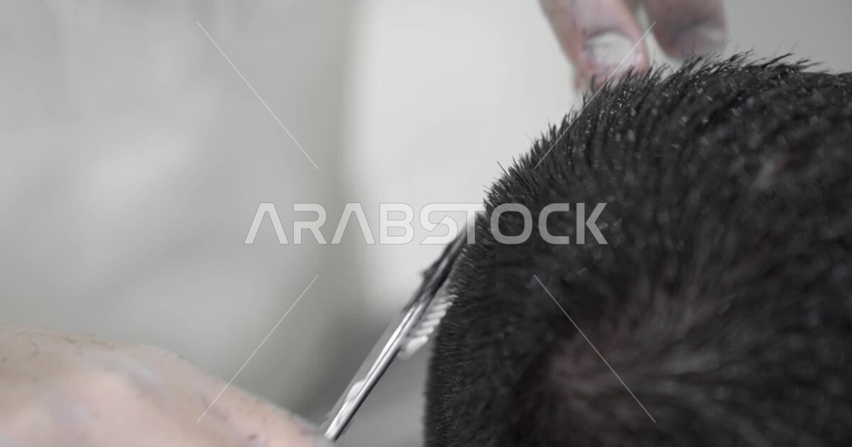 A Saudi Arabian Gulf man visits a barber shop. The barber uses the ...