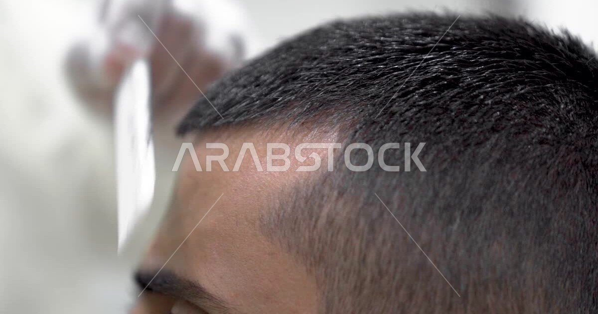 A Saudi Arabian Gulf man visits a barber shop. The barber uses the ...