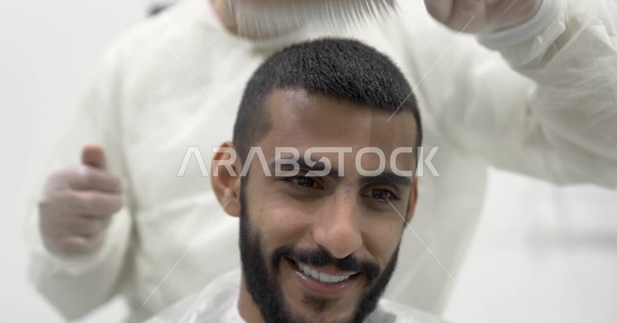 A Saudi Arabian Gulf man visits a barber shop. The barber uses the ...