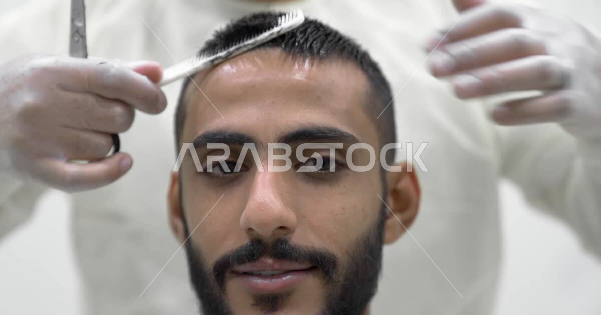 A Saudi Arabian Gulf man visits a barber shop. The barber uses the ...