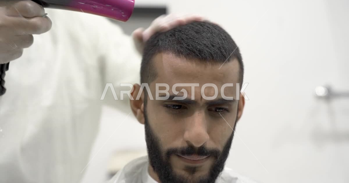 A Saudi Arabian Gulf man visits a barber shop. The barber uses the ...