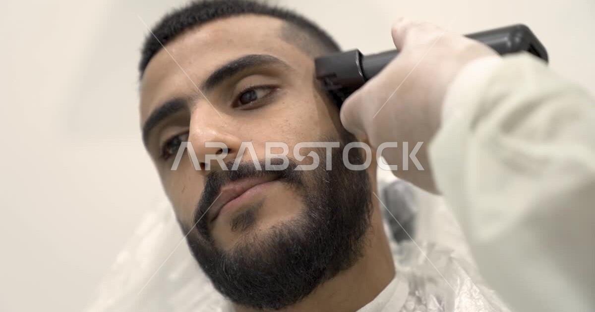 A Saudi Arabian Gulf man visits a hairdressing salon. The barber takes ...