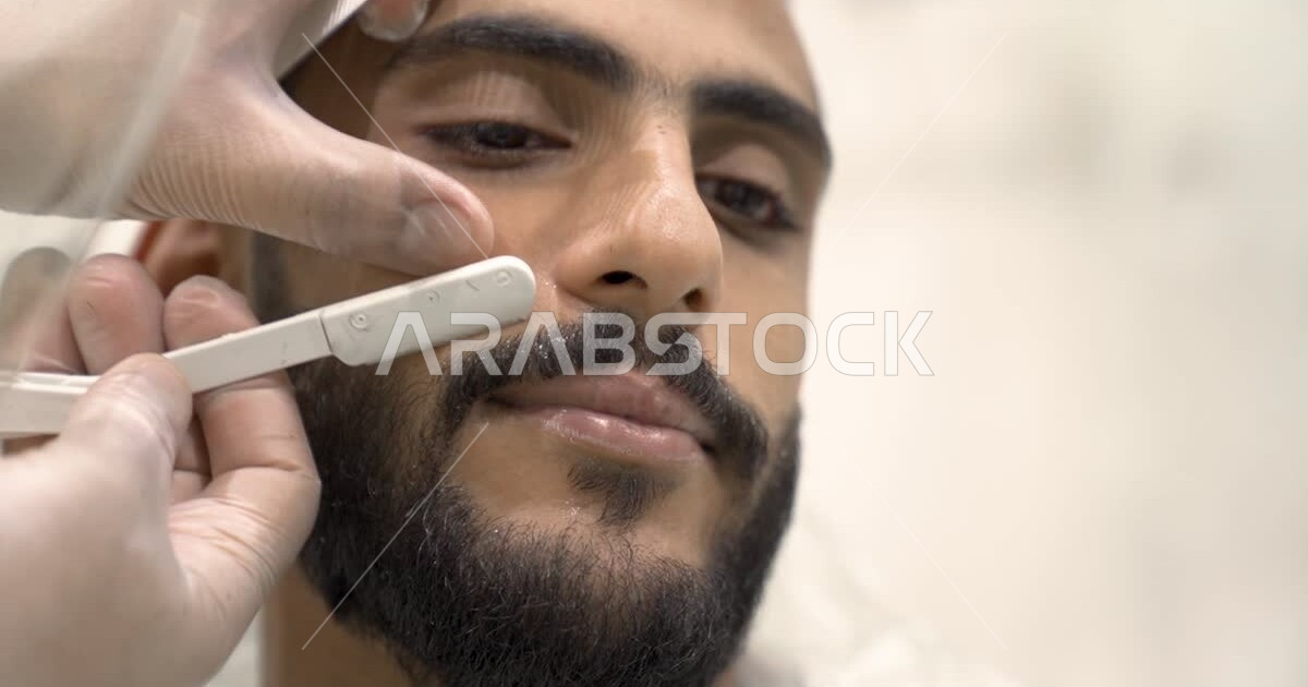 A Saudi Arabian Gulf man visits a hairdressing salon. The barber takes ...