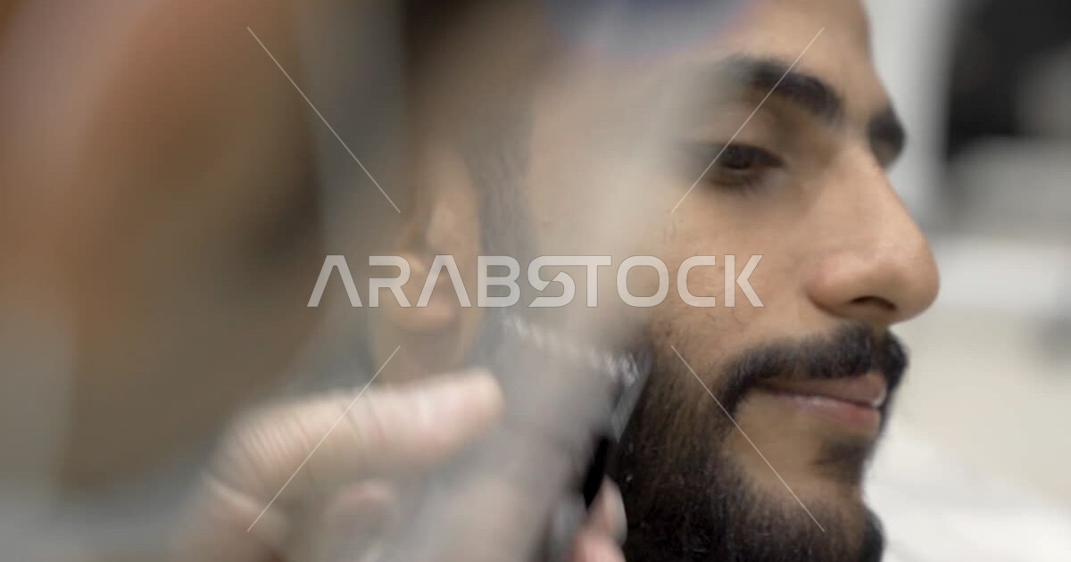 A Saudi Arabian Gulf man visits a hairdressing salon. The barber takes ...