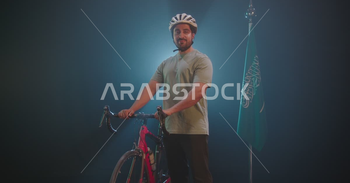 Standing next to the Saudi flag, a Saudi Gulf Arab man holding a ...