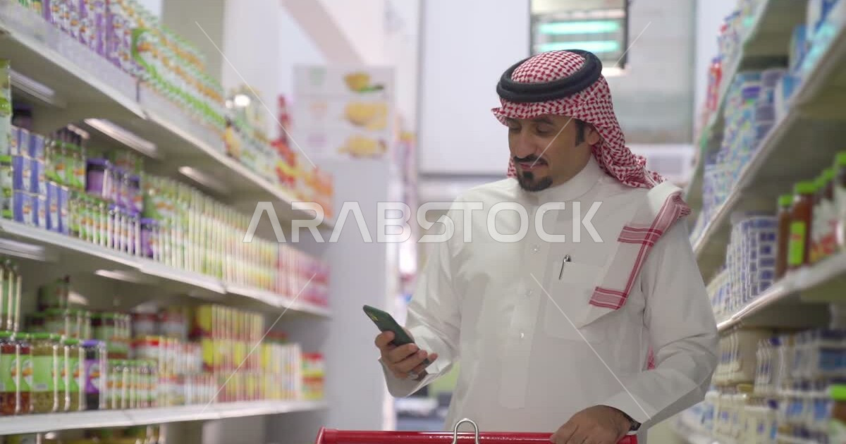 A Saudi-Gulf man shopping in the supermarket, with his mobile phone ...