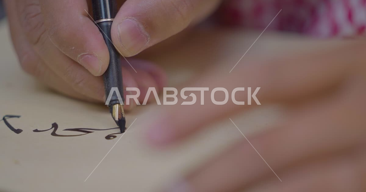 A man writing a traditional Arabic manuscript, a close-up of the hand ...