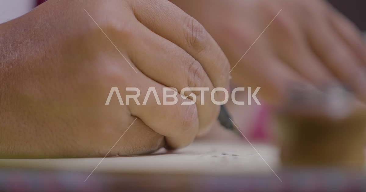 A man writing a traditional Arabic manuscript, a close-up of the hand ...