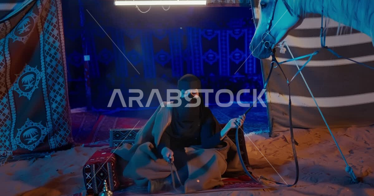 A Saudi Arabian Gulf woman wearing a fur and burqa stirs coals using ...