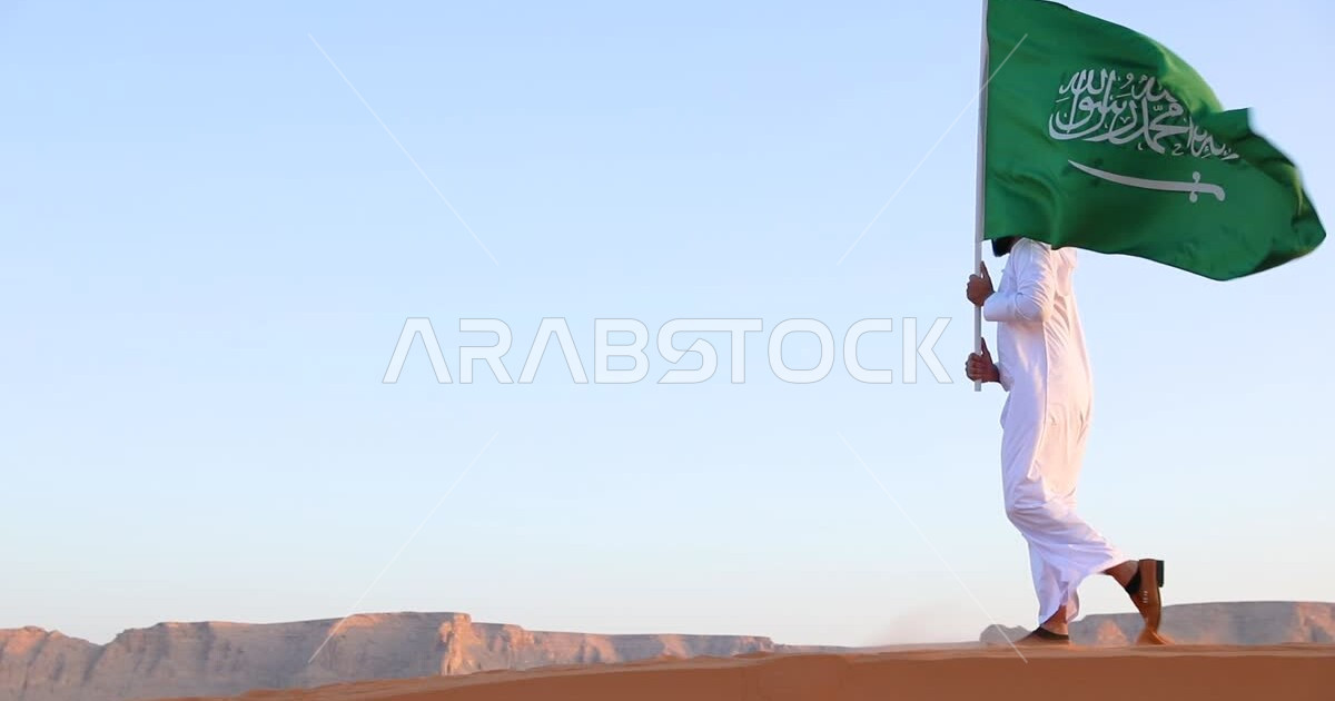 A Saudi man carries the Saudi flag over the hills of one of the desert ...