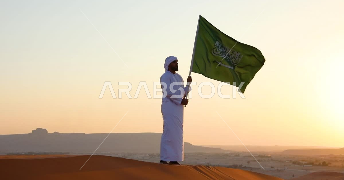 A Saudi man carries the Saudi flag over the hills of one of the desert ...