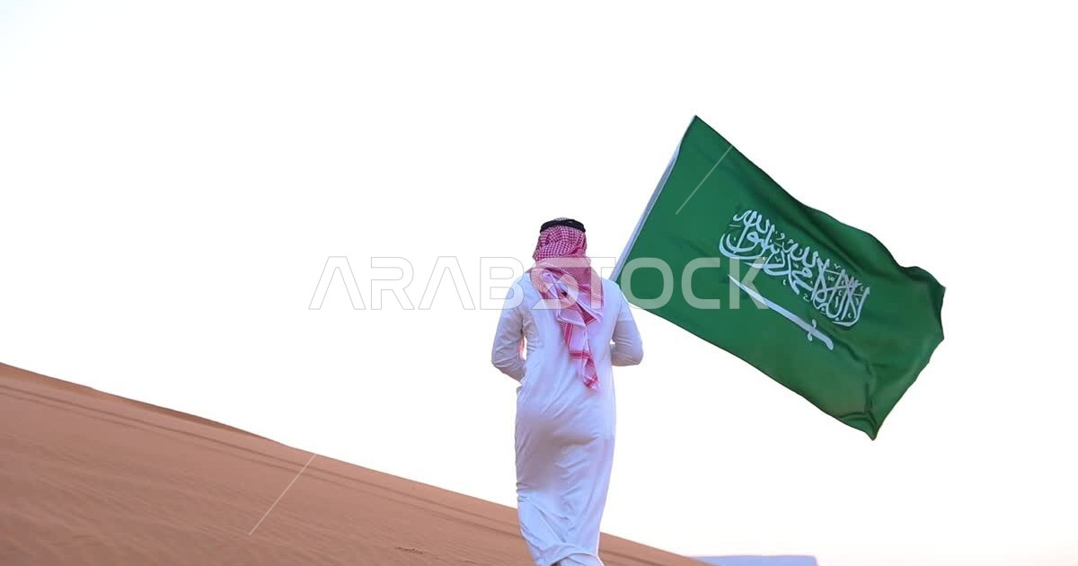 A Saudi man carries the Saudi flag over the hills of one of the desert ...