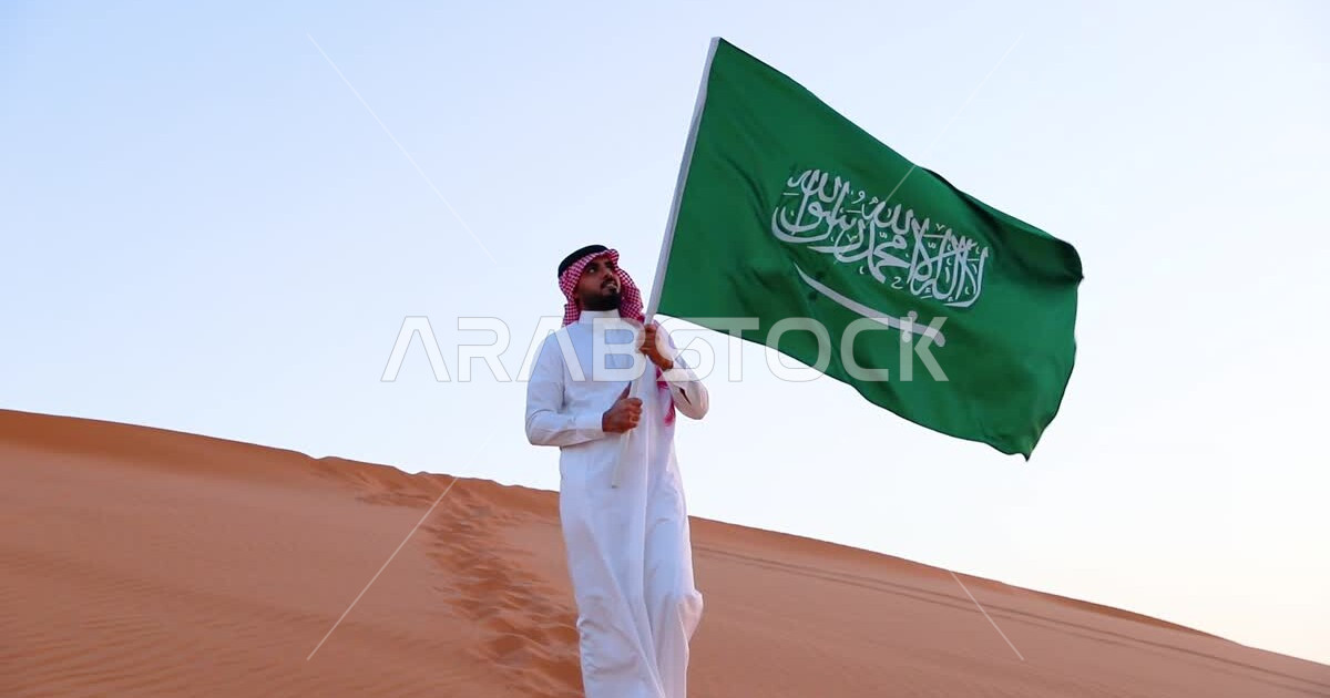 A Saudi man carries the Saudi flag over the hills of one of the desert ...