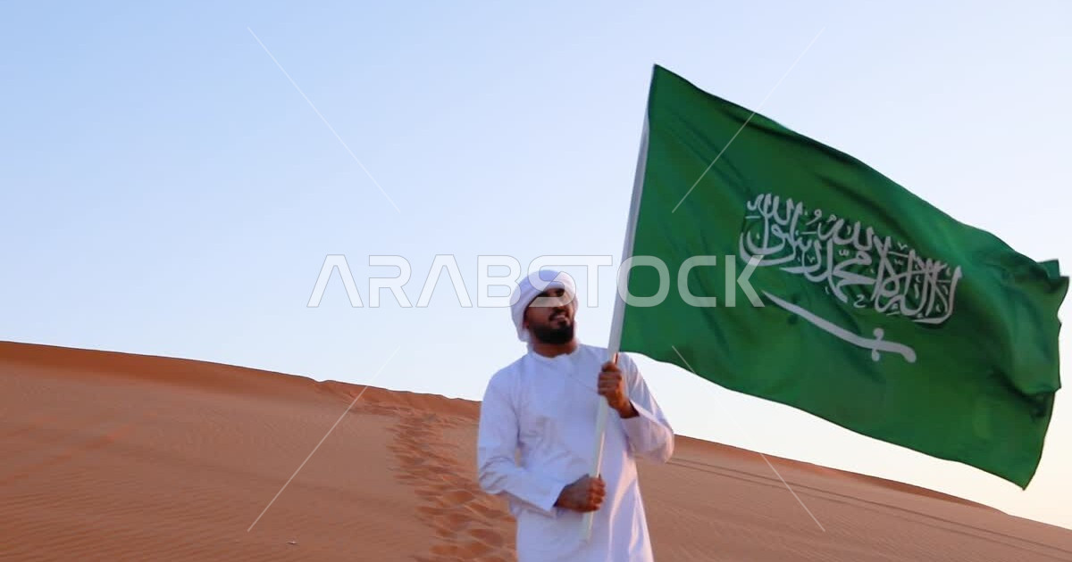 A Saudi man carries the Saudi flag over the hills of one of the desert ...